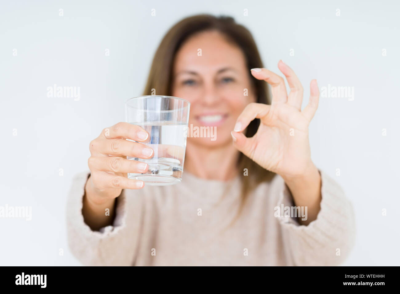 Middle age woman drinking glass of water isolated background doing ok ...