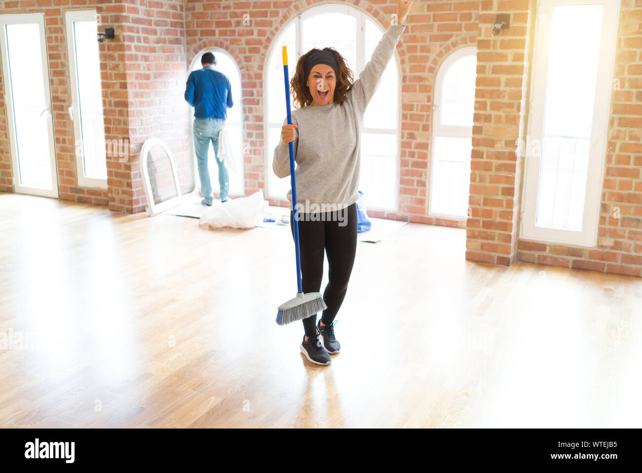 Middle age woman with curly hair working cleaning the house using a ...