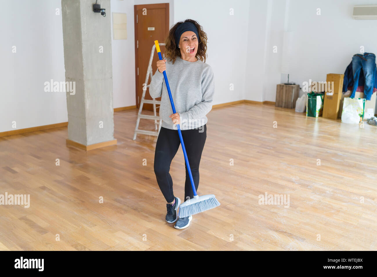 Middle age woman with curly hair working cleaning the house using a ...
