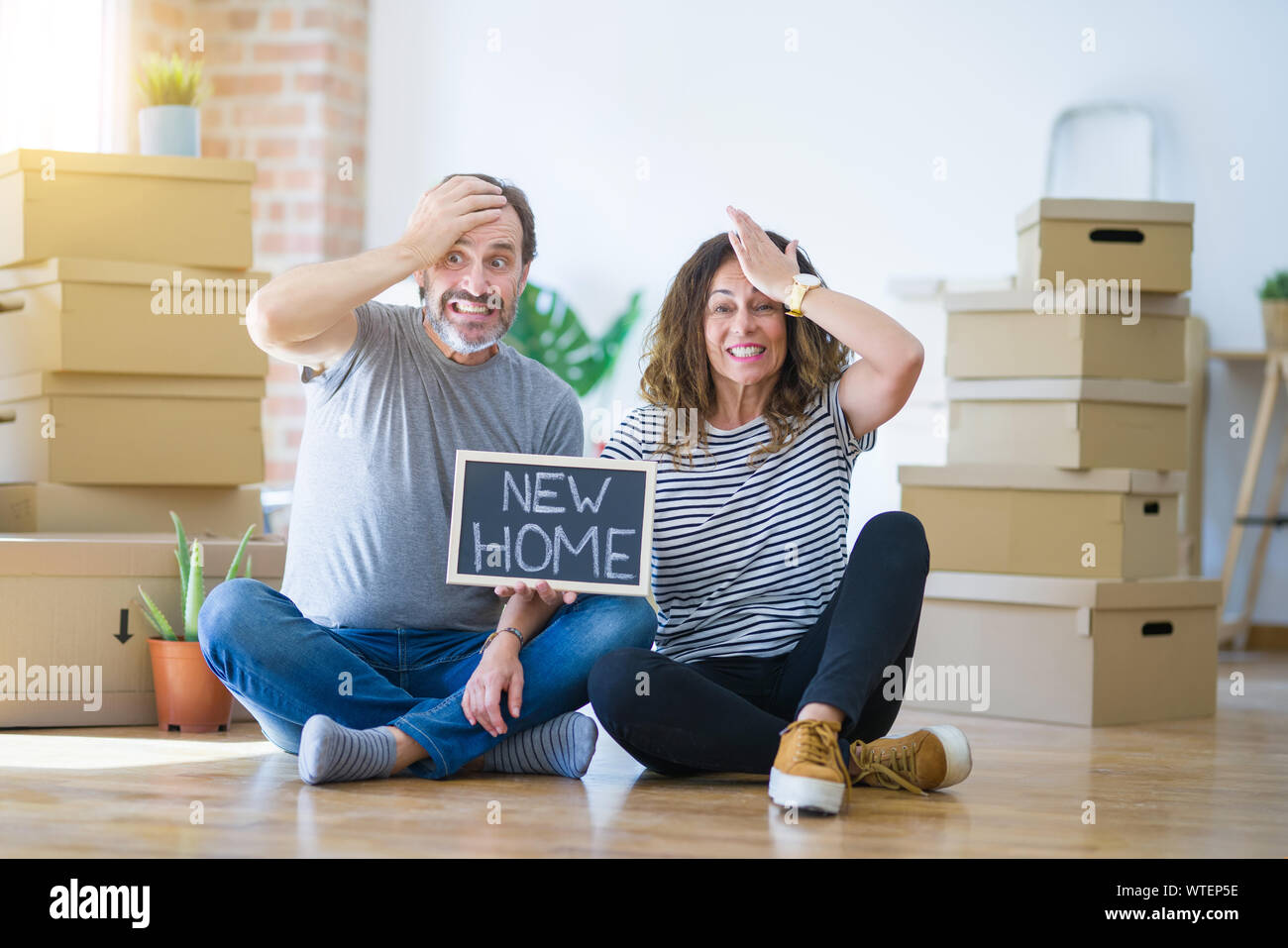 Middle age senior couple sitting on the floor holding blackboard moving ...