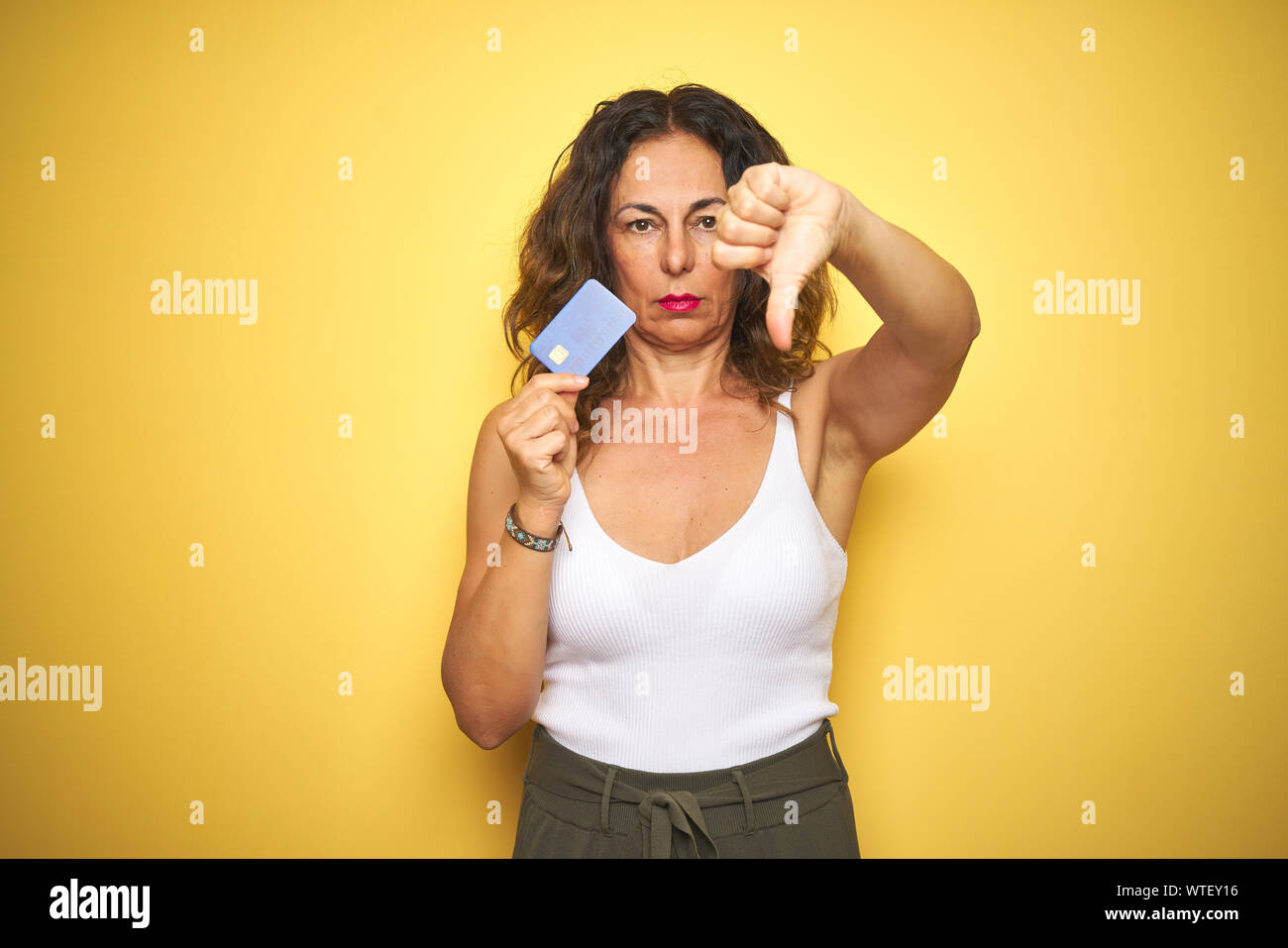 Middle age senior woman holding credit card over yellow isolated ...