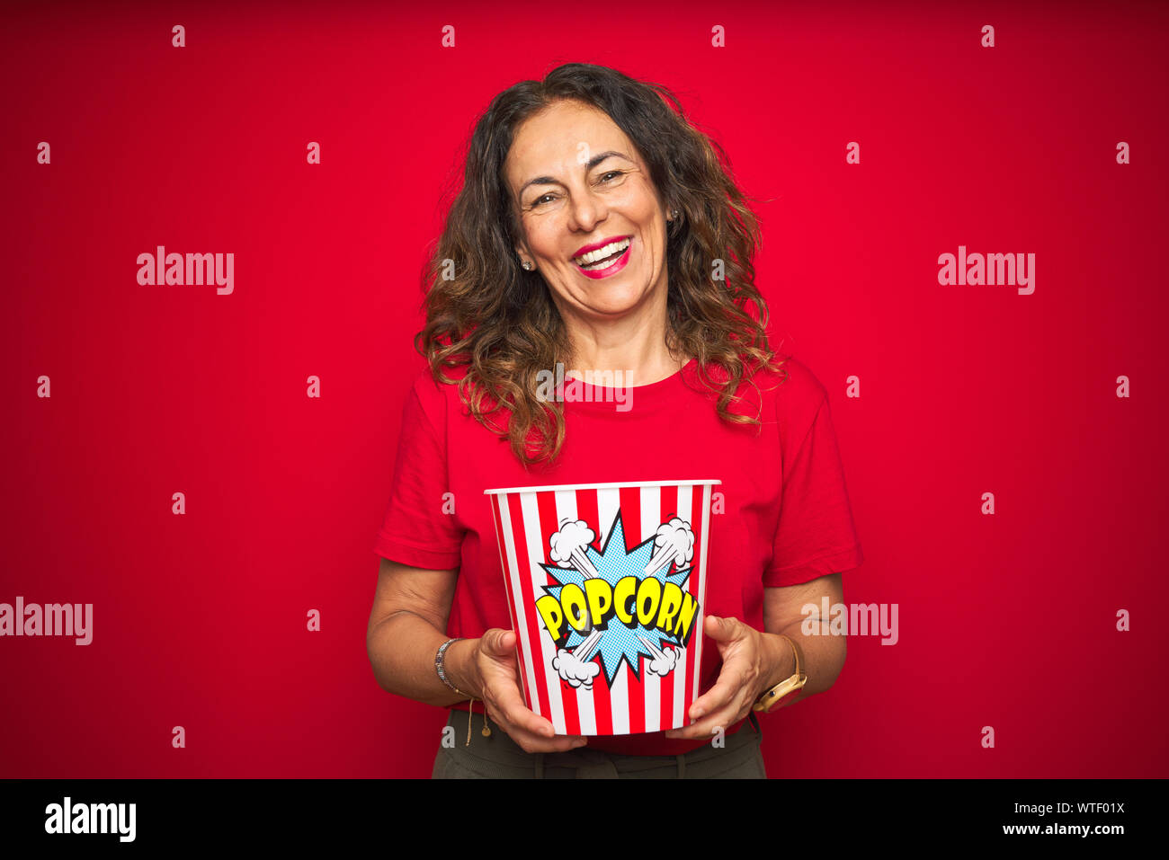 Middle age senior woman eating popcorn snack over red isolated ...