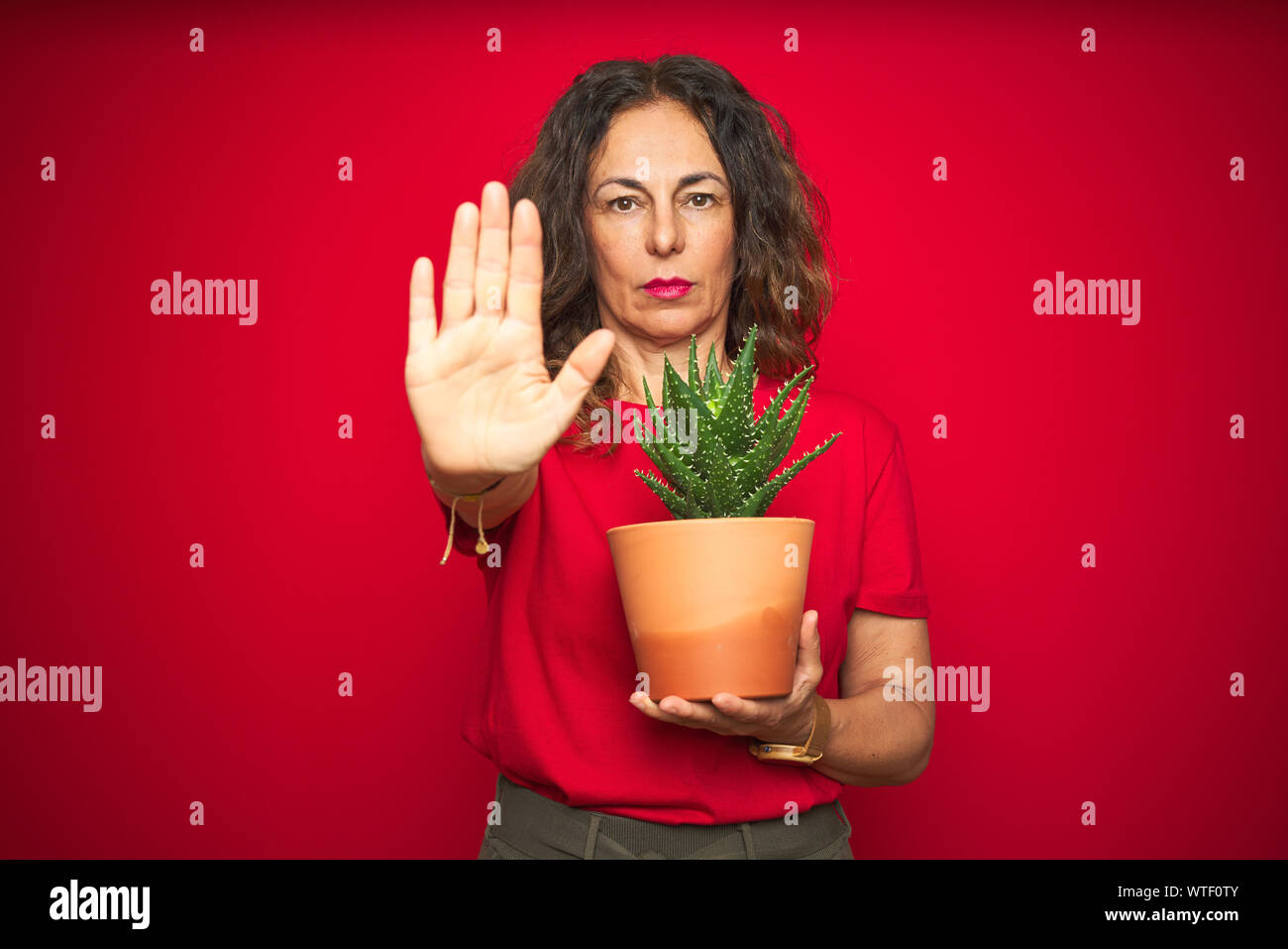 Middle age senior woman holding green cactus over red isolated background with open hand doing ...