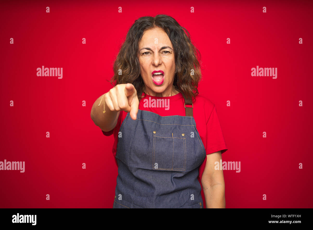 Middle age senior woman wearing apron uniform over red isolated ...