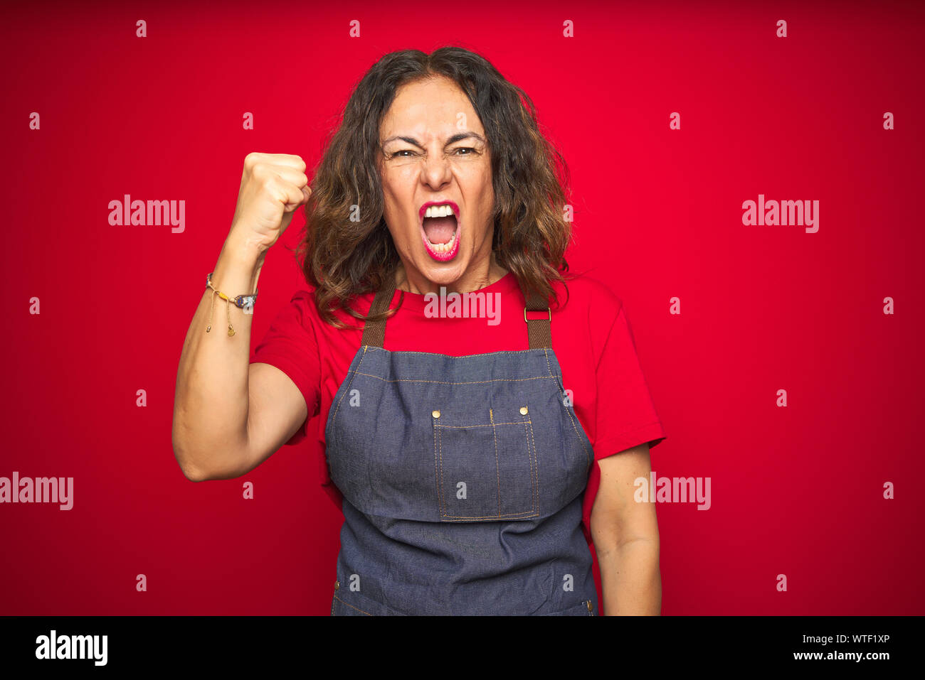 Middle age senior woman wearing apron uniform over red isolated ...