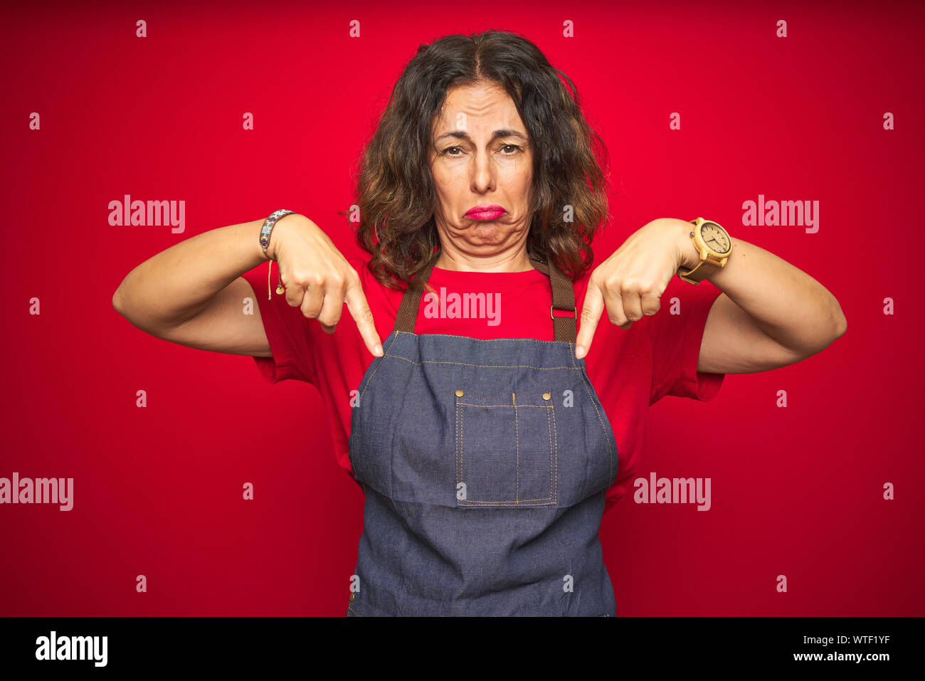 Middle age senior woman wearing apron uniform over red isolated ...