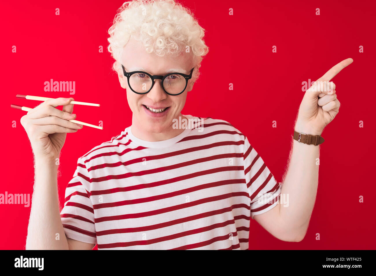 Young albino blond man holding chopsticks standing over isolated white ...