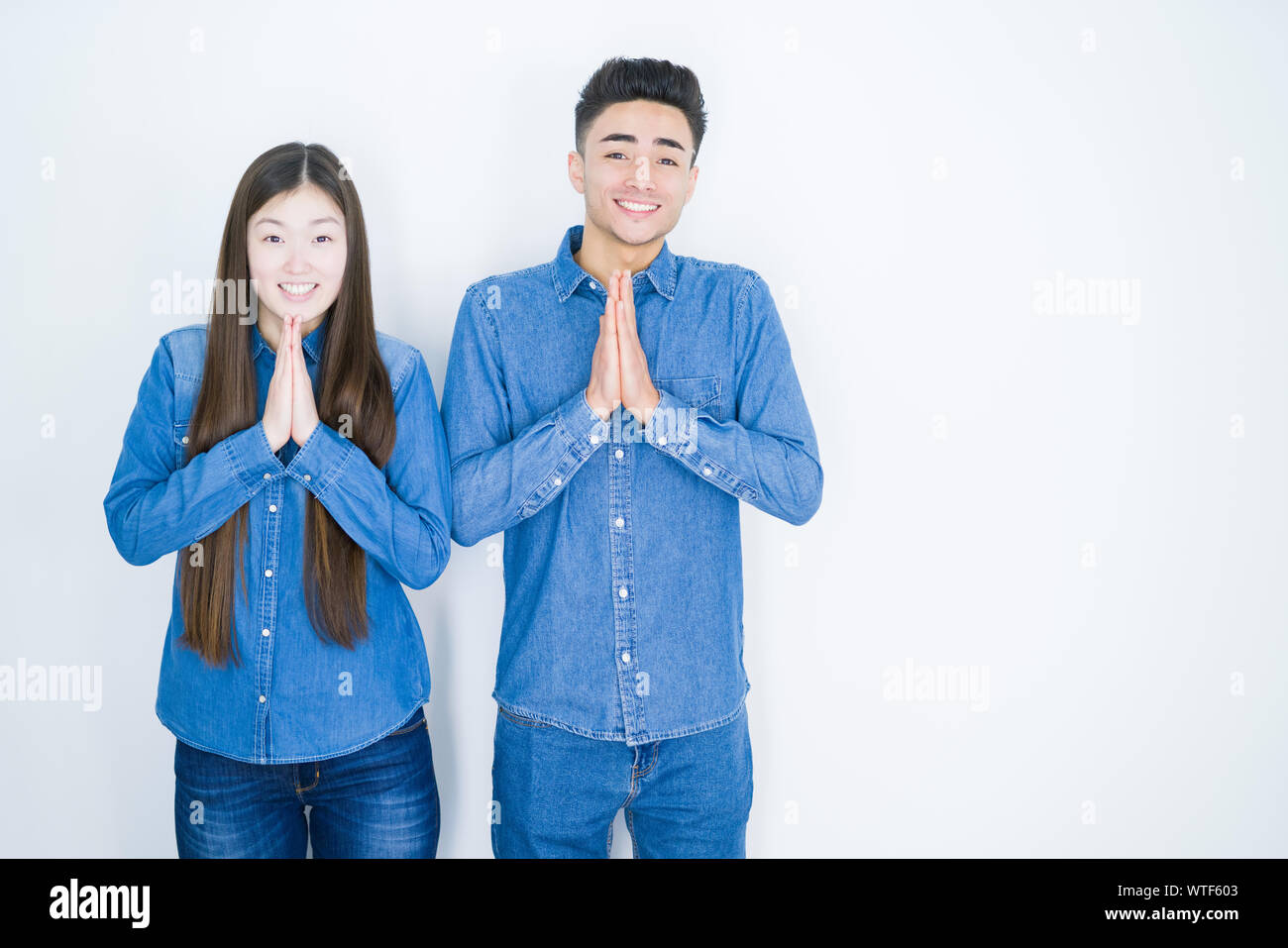 Beautiful young asian couple over white isolated background praying ...