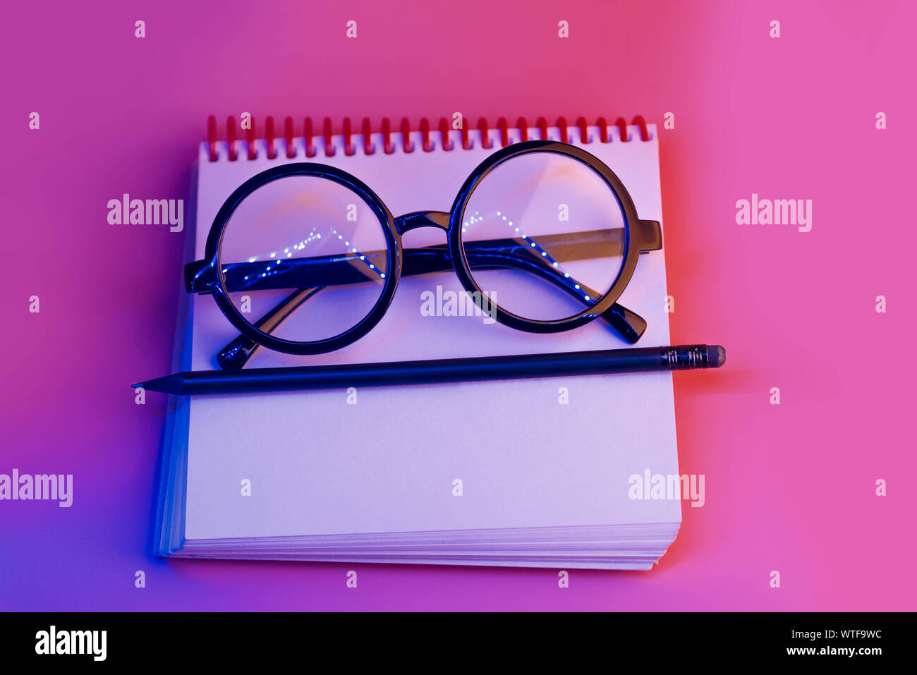 black round glasses lie on a Notepad in neon light on a pink background ...