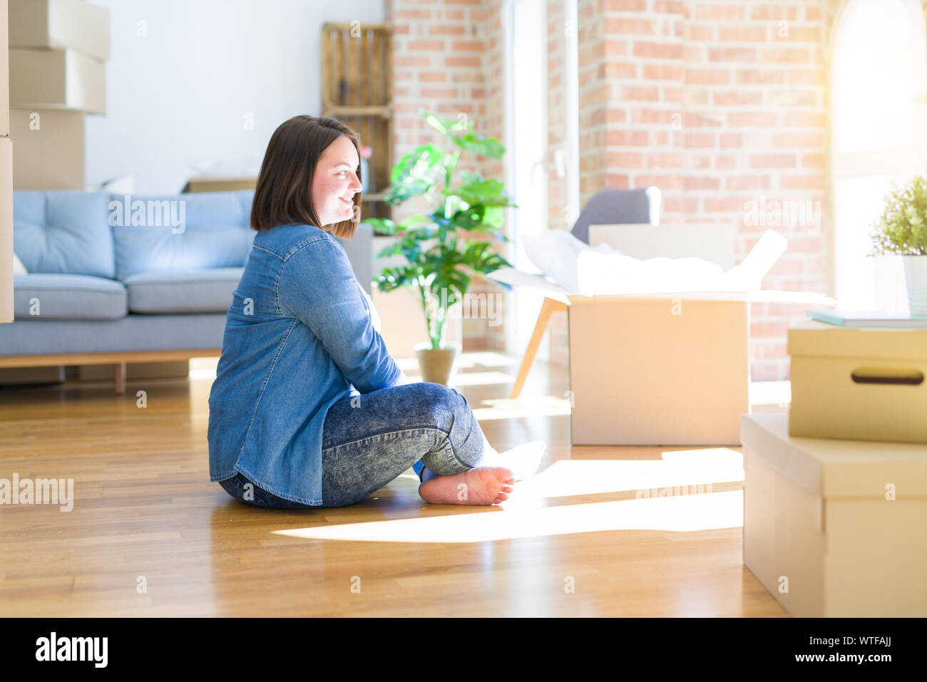 Young plus size woman sitting on the floor around cardboard boxes ...