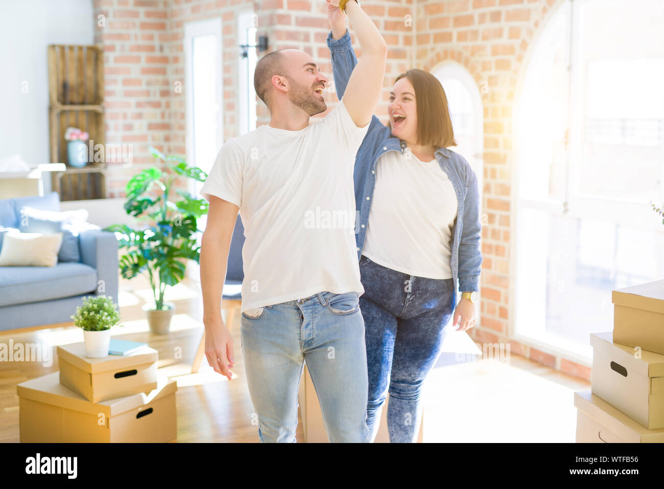 Young couple dancing around cardboard boxes at new home, celebrating ...
