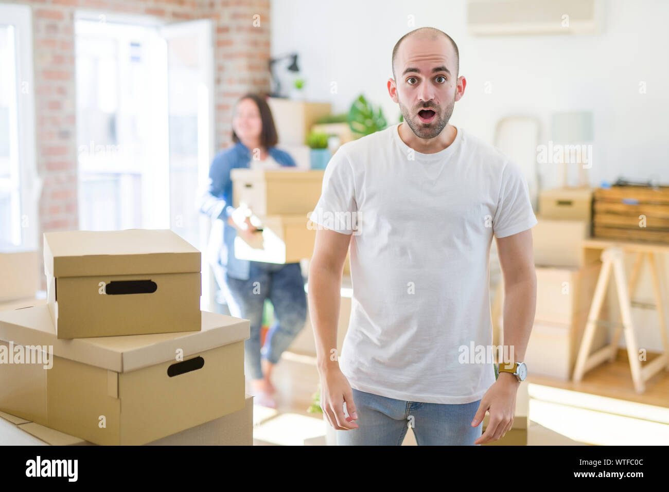 Young couple arround cardboard boxes moving to a new house, bald man ...