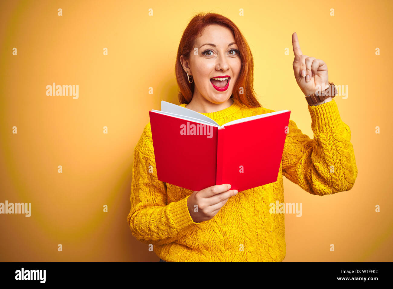 Young redhead teacher woman reading red book over yellow isolated ...