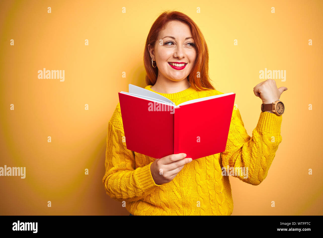 Young redhead teacher woman reading red book over yellow isolated ...