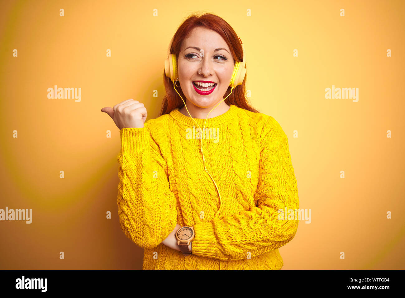 Young redhead woman listening to music using headphones over yellow ...