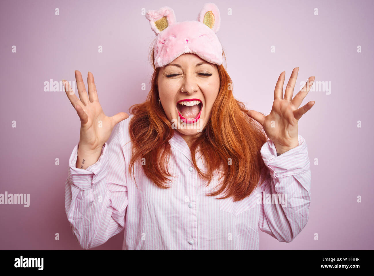 Young beautiful redhead woman wearing pajama over pink isolated background celebrating mad and ...