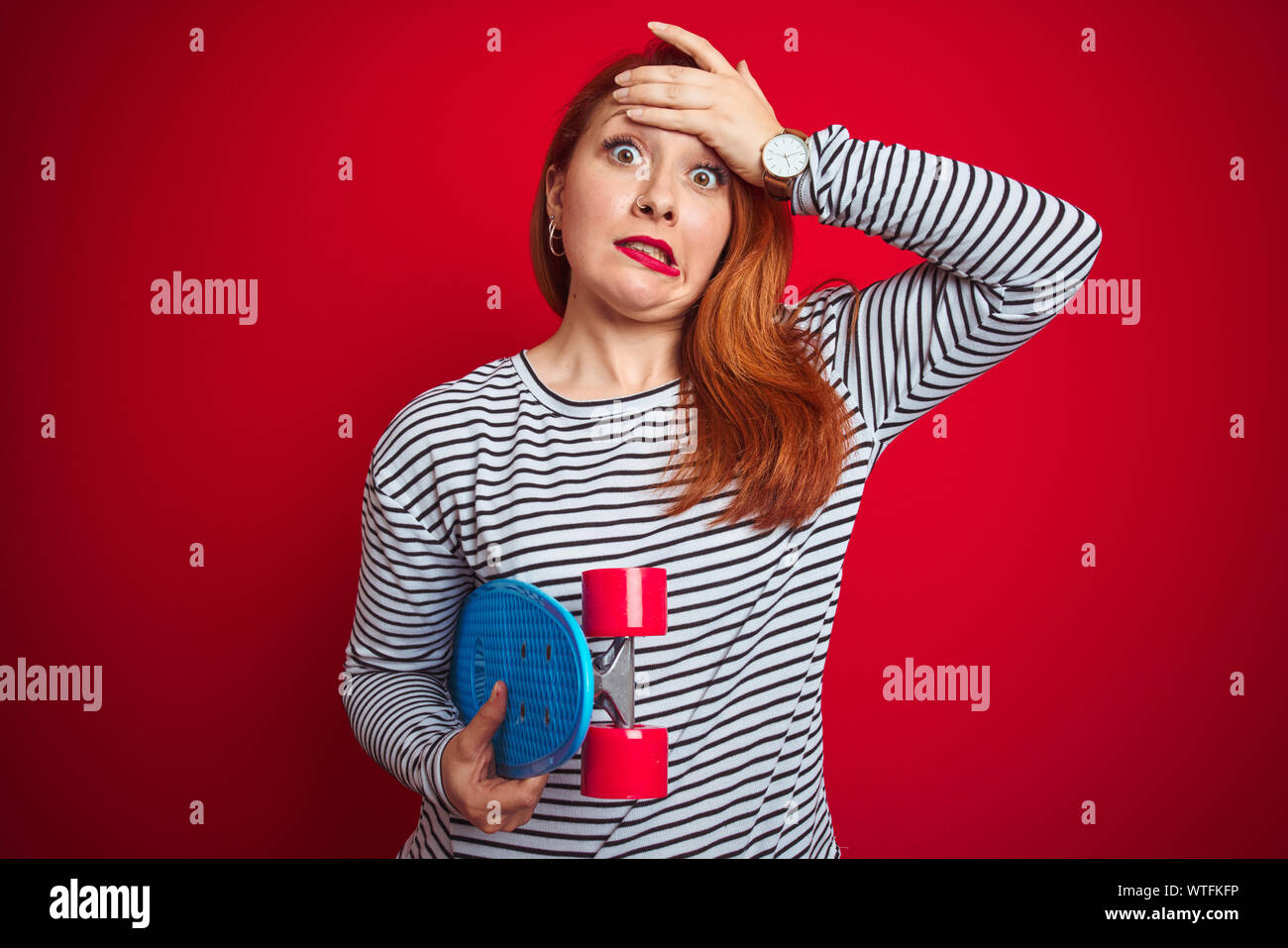 Young redhead student woman holding skate over red isolated background ...