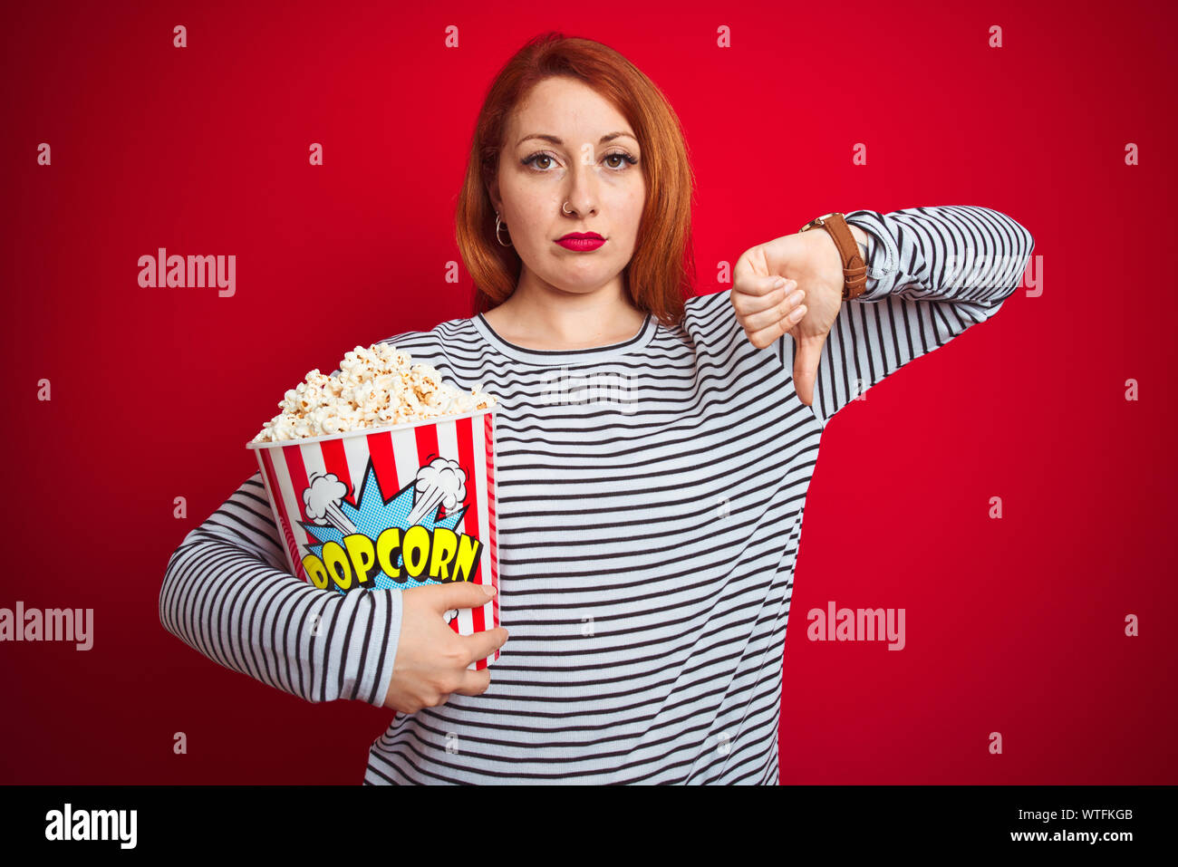 Young beautiful redhead woman eating popcorn over red isolated ...