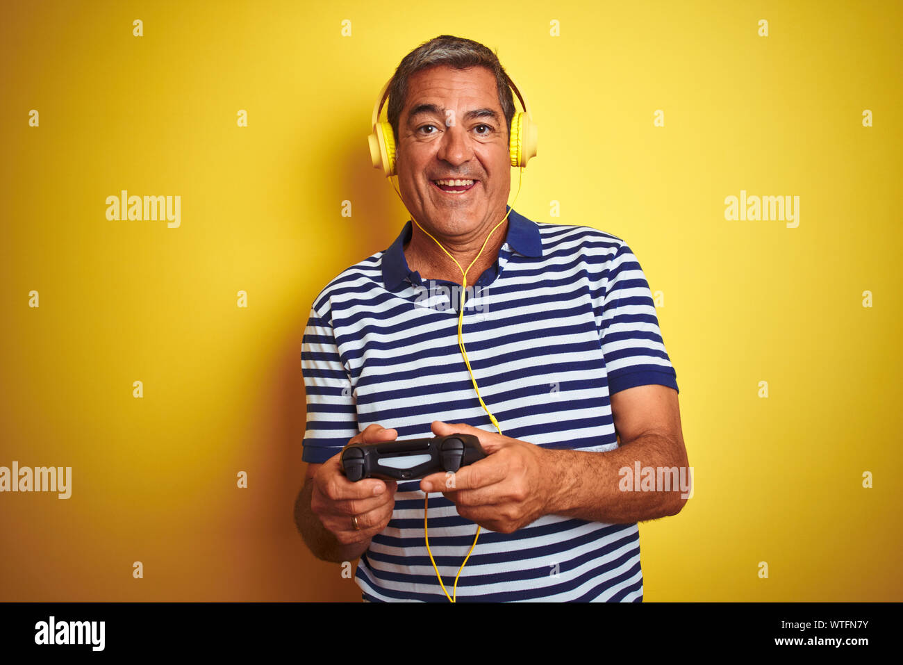 Middle age man playing video game using headphones over isolated yellow ...