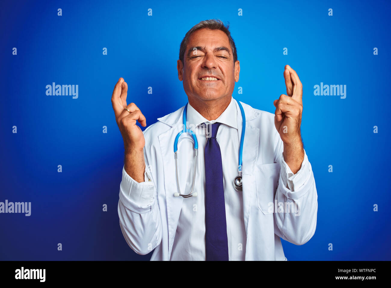 Handsome middle age doctor man wearing stethoscope over isolated blue ...