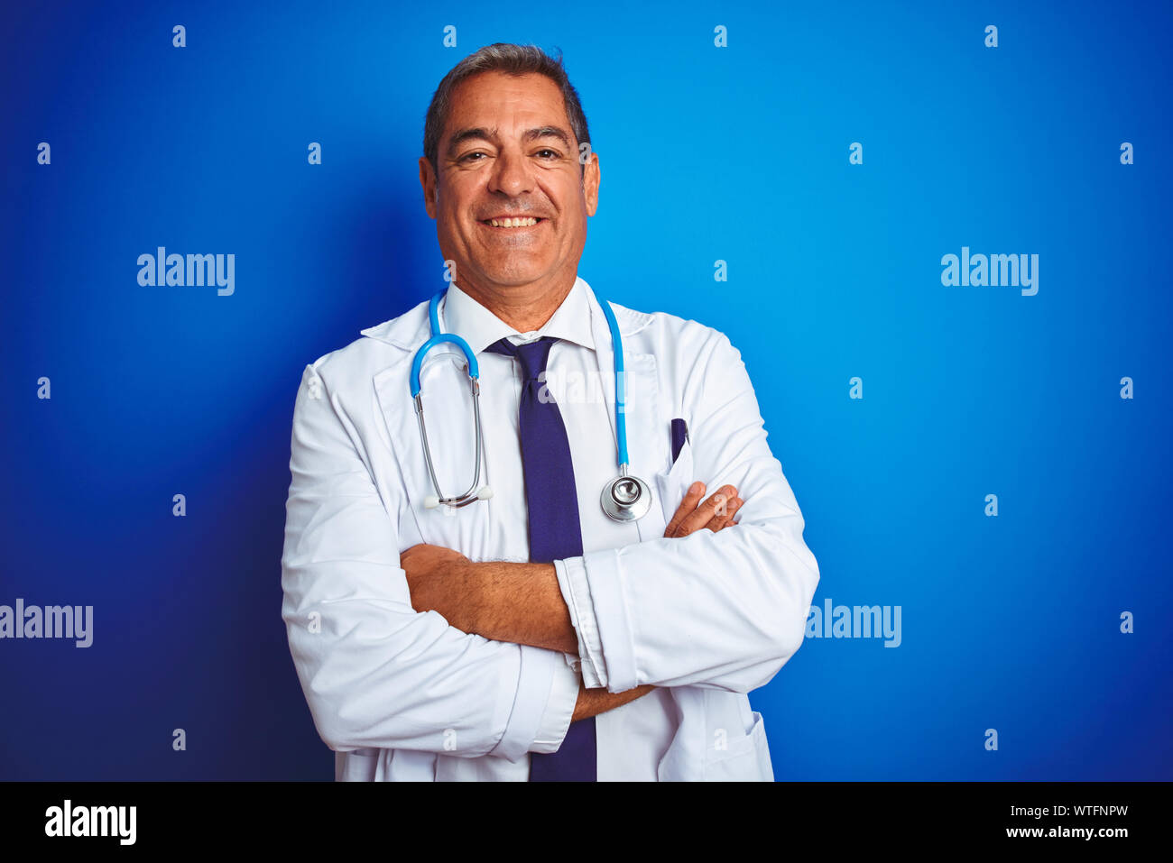 Handsome middle age doctor man wearing stethoscope over isolated blue ...