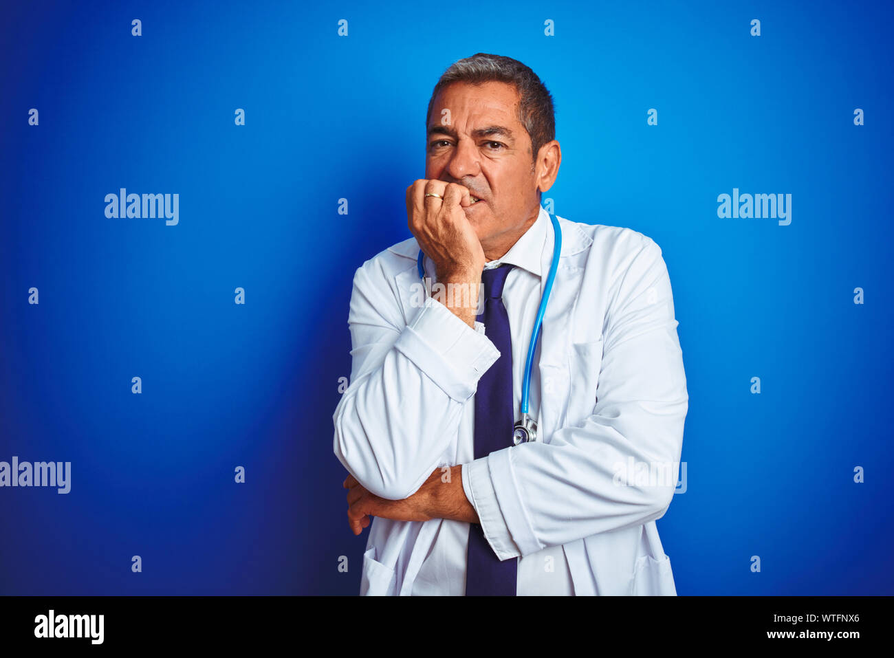 Handsome middle age doctor man wearing stethoscope over isolated blue ...