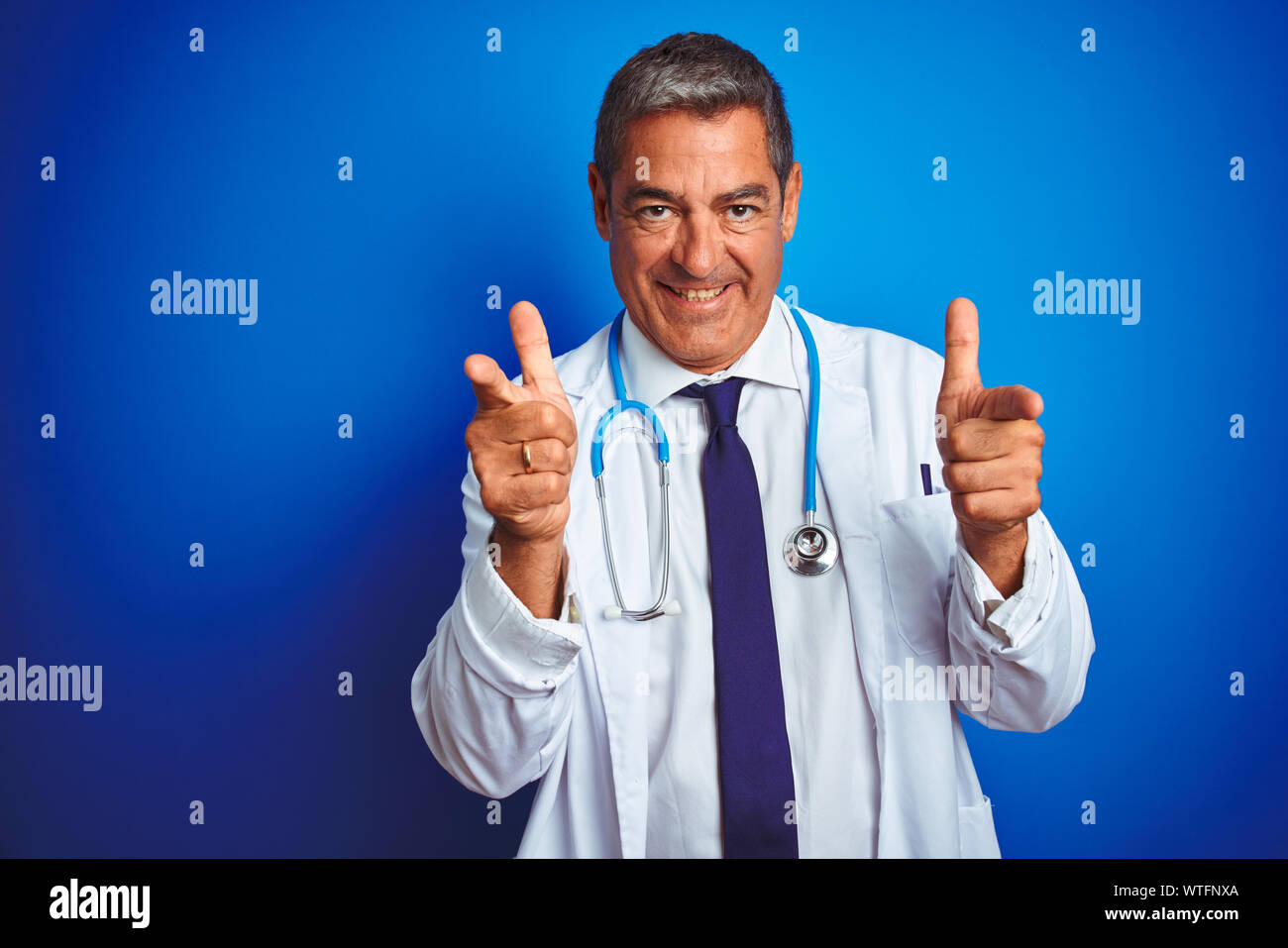 Handsome middle age doctor man wearing stethoscope over isolated blue ...