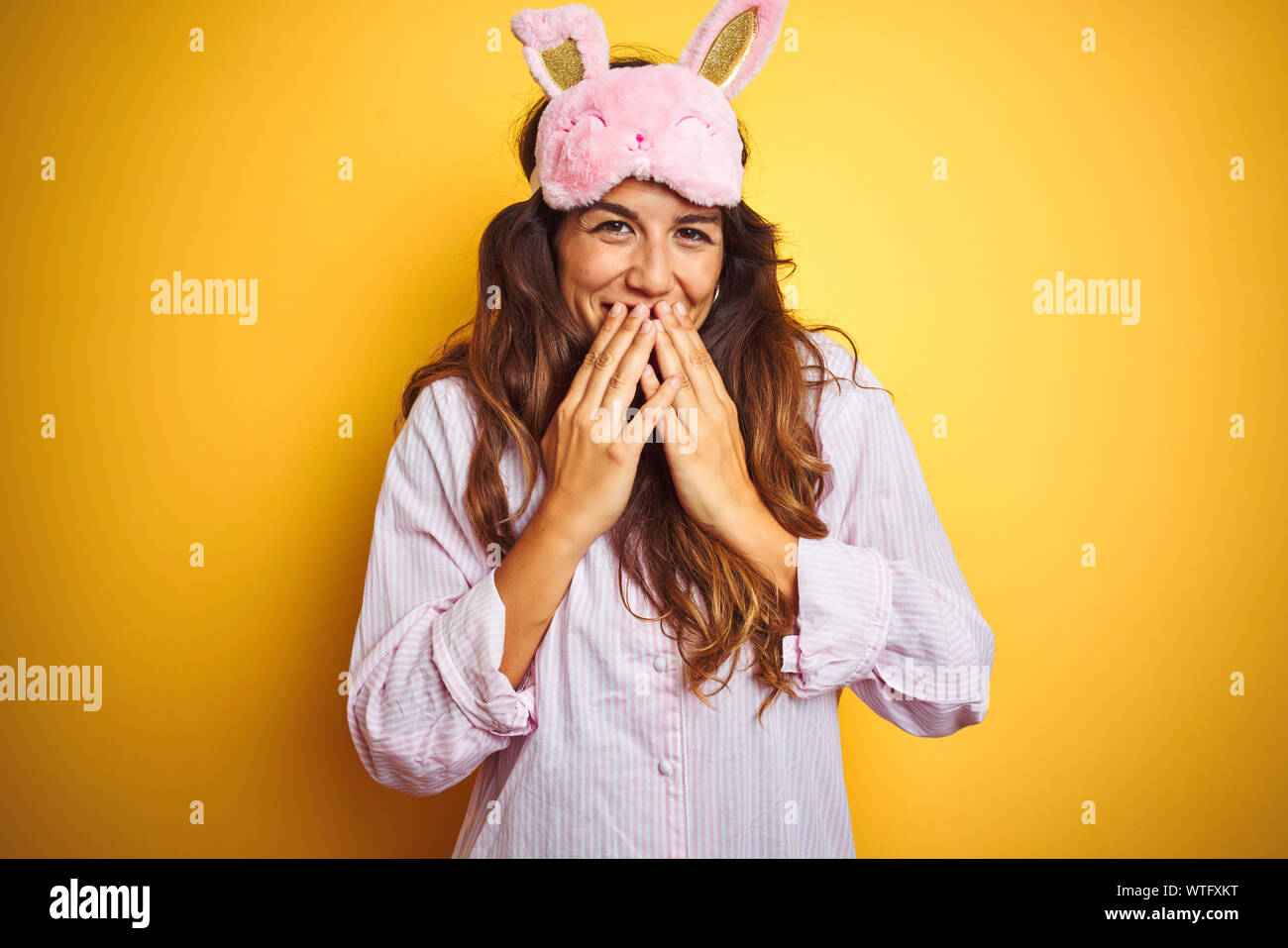 Young woman wearing pajama and sleep mask standing over yellow isolated ...
