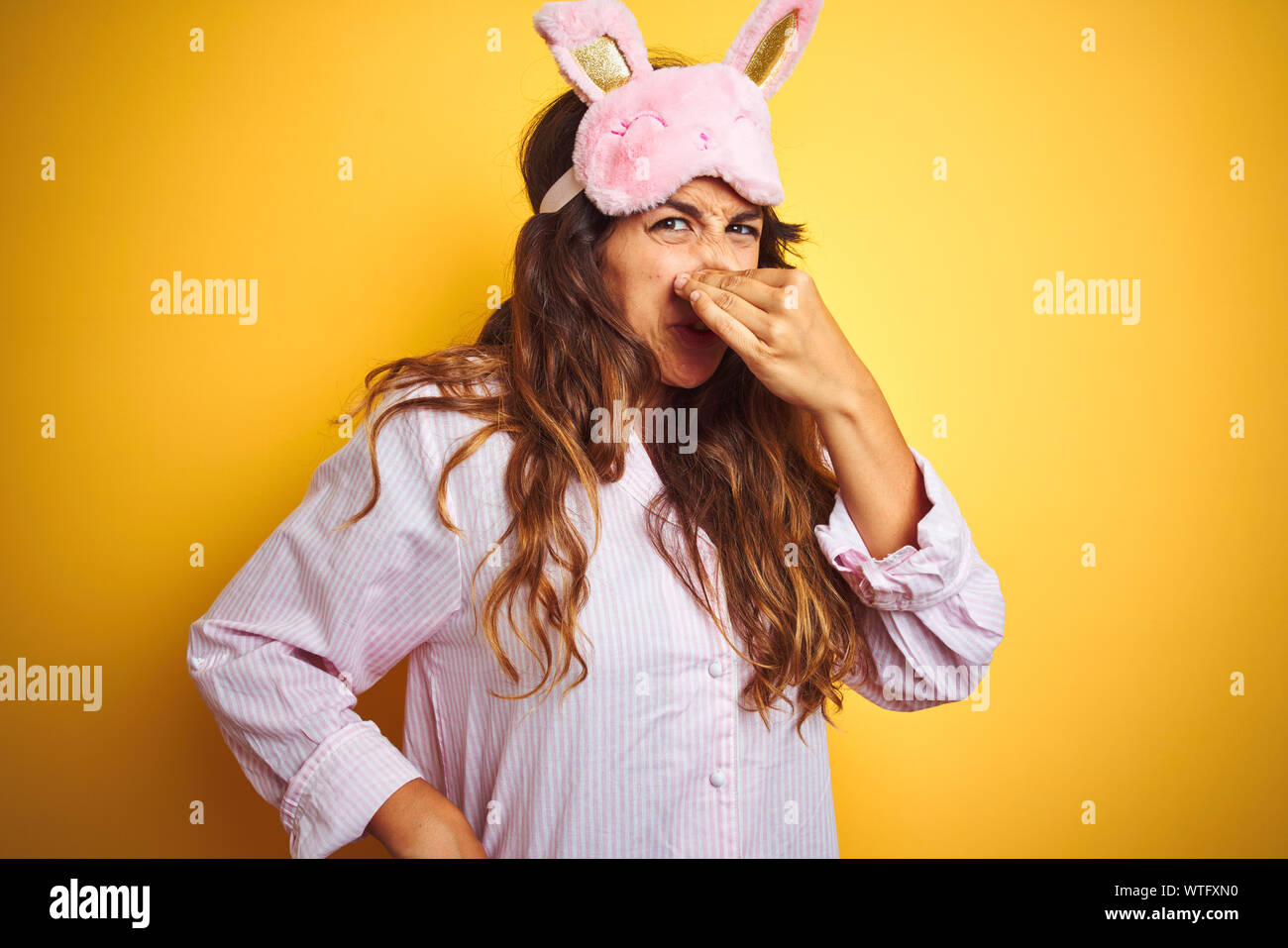 Young woman wearing pajama and sleep mask standing over yellow isolated ...