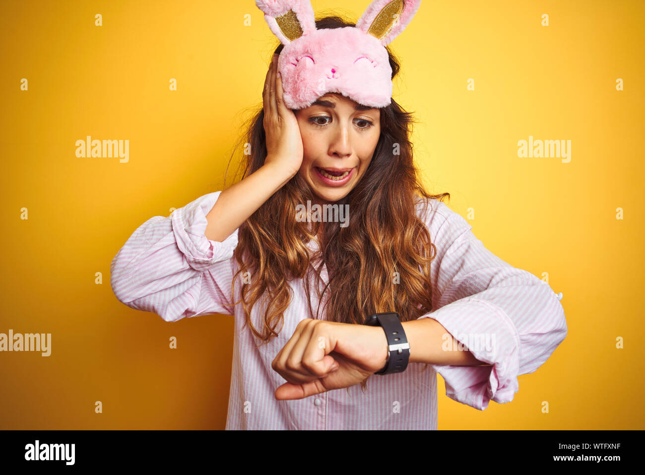 Young woman wearing pajama and sleep mask standing over yellow isolated ...