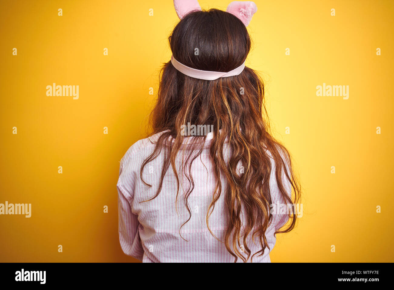 Young woman wearing pajama and sleep mask standing over yellow isolated ...