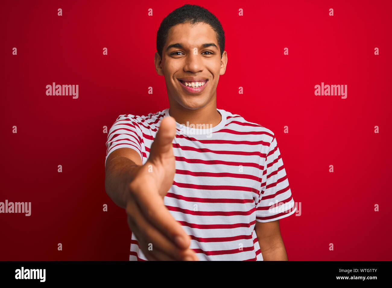 Young Handsome Arab Man Wearing Striped T Shirt Over Isolated Red