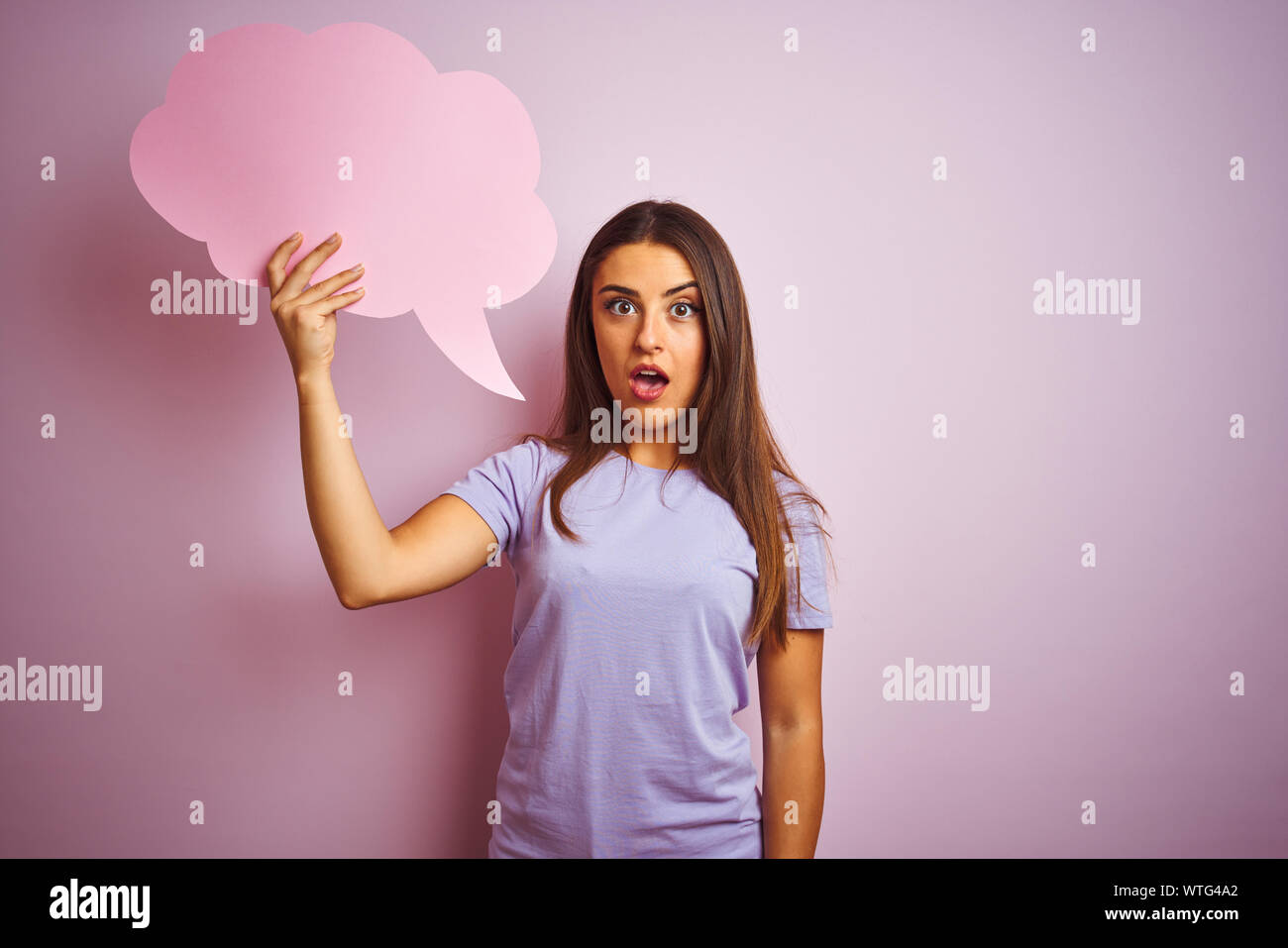 Young beautiful woman holding cloud speech bubble over isolated pink ...