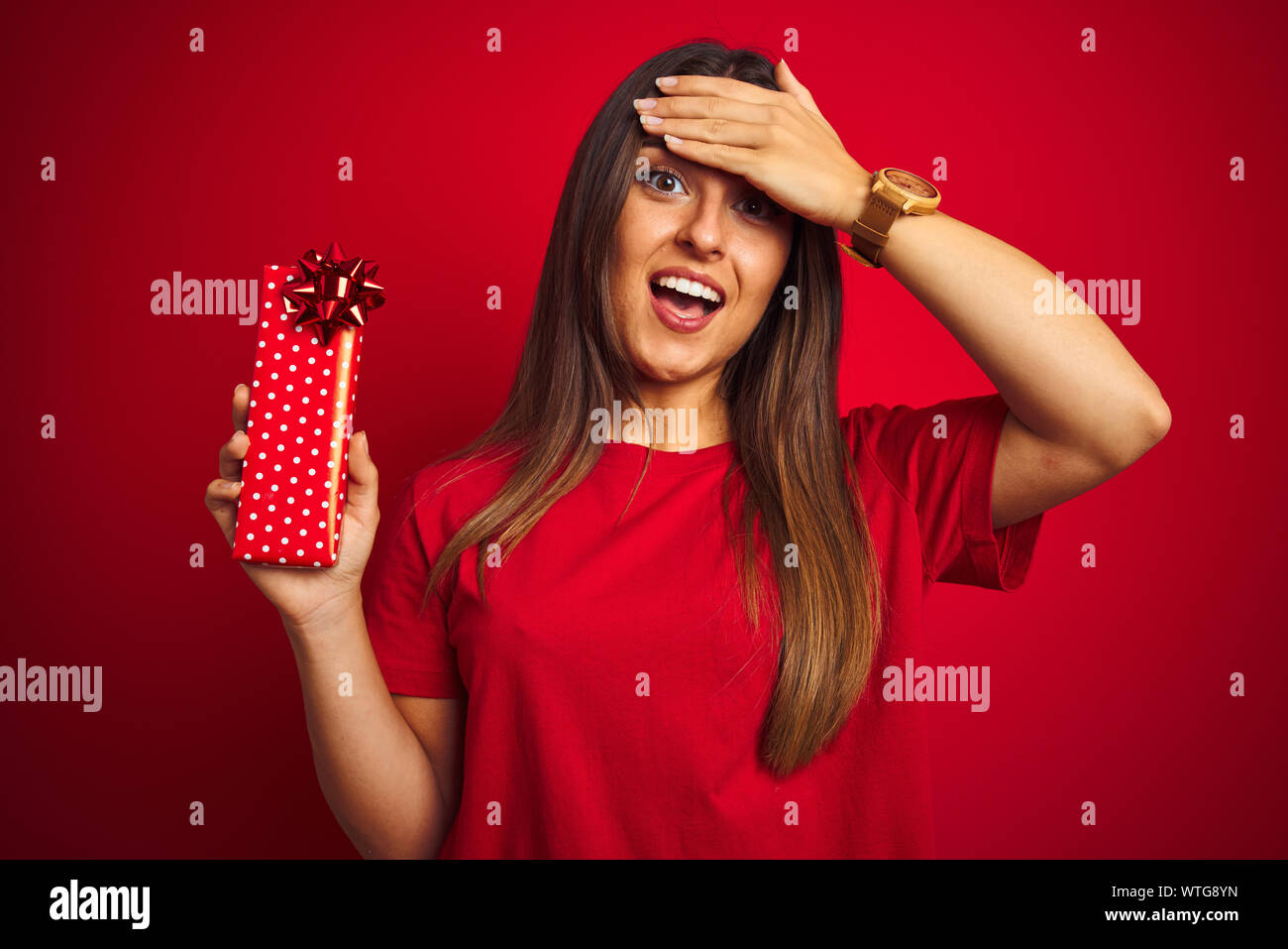 Young beautiful woman holding birthday gift standing over isolated red ...