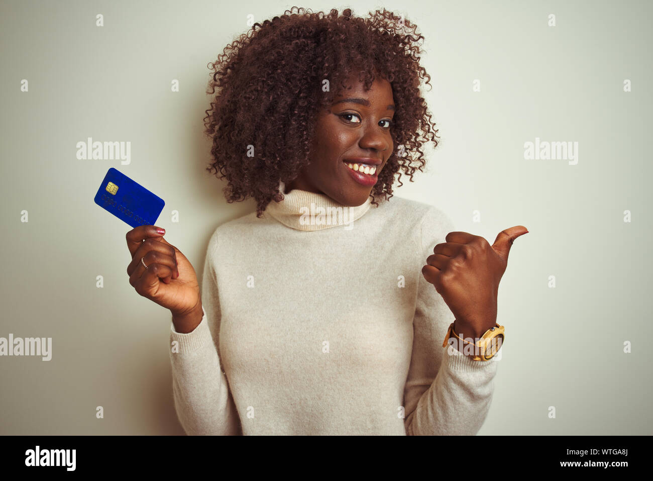 Young african afro woman holding credit card standing over isolated white background pointing ...