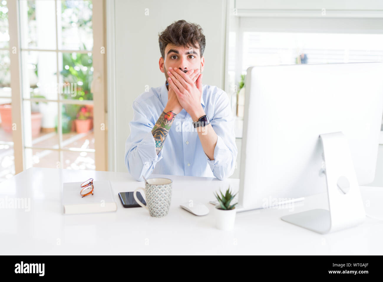 Young business man working using computer shocked covering mouth with ...