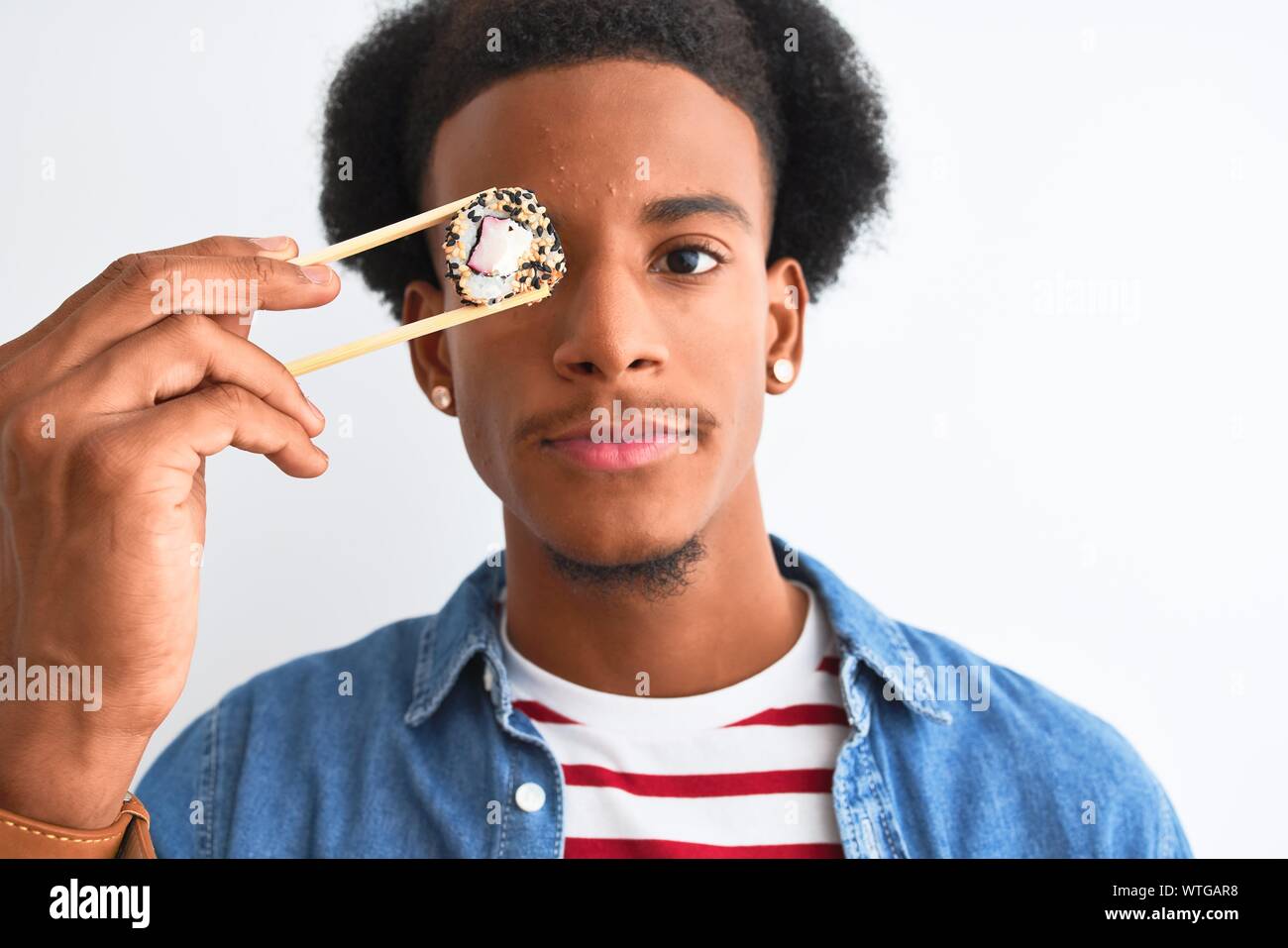 Young african american man eating sushi using chopsticks over isolated ...
