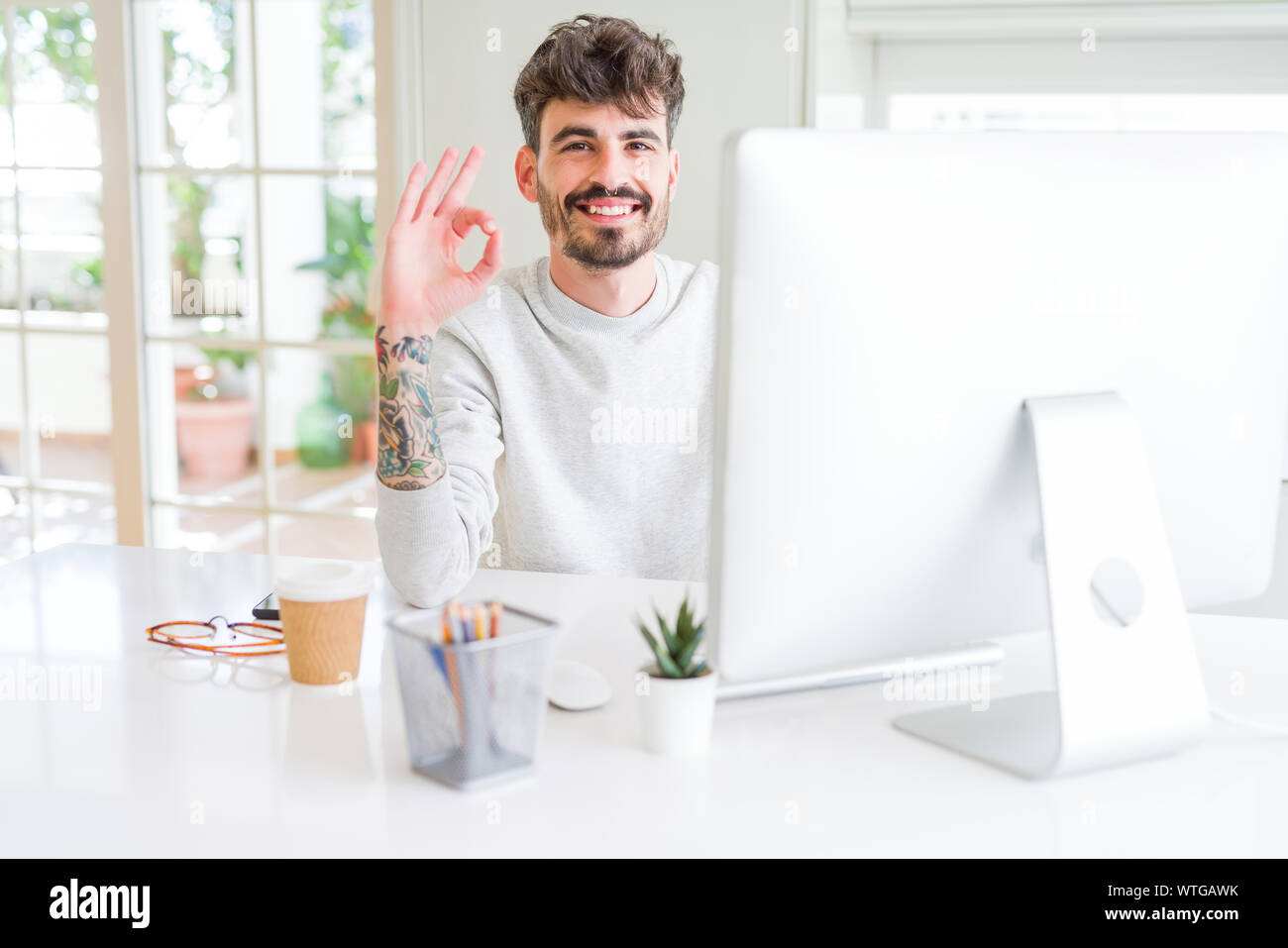 Young man working using computer doing ok sign with fingers, excellent ...