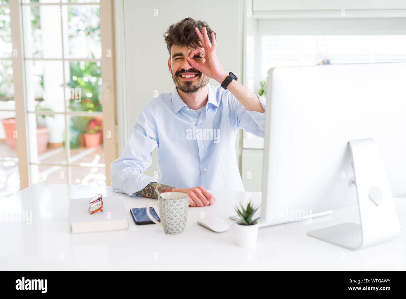 Young business man working using computer doing ok gesture with hand ...