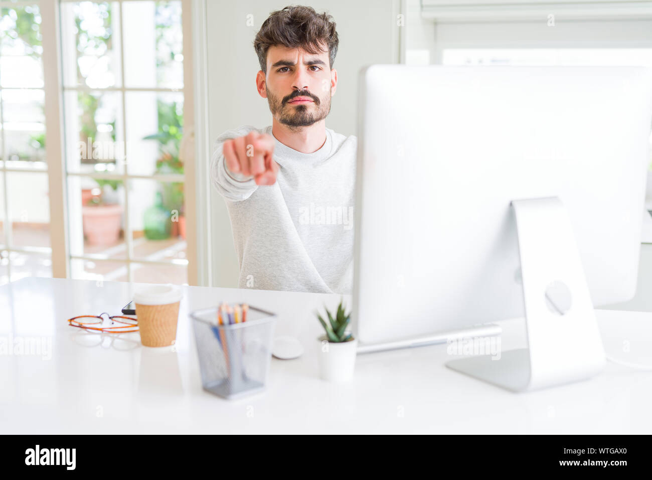 Young man working using computer pointing with finger to the camera and ...