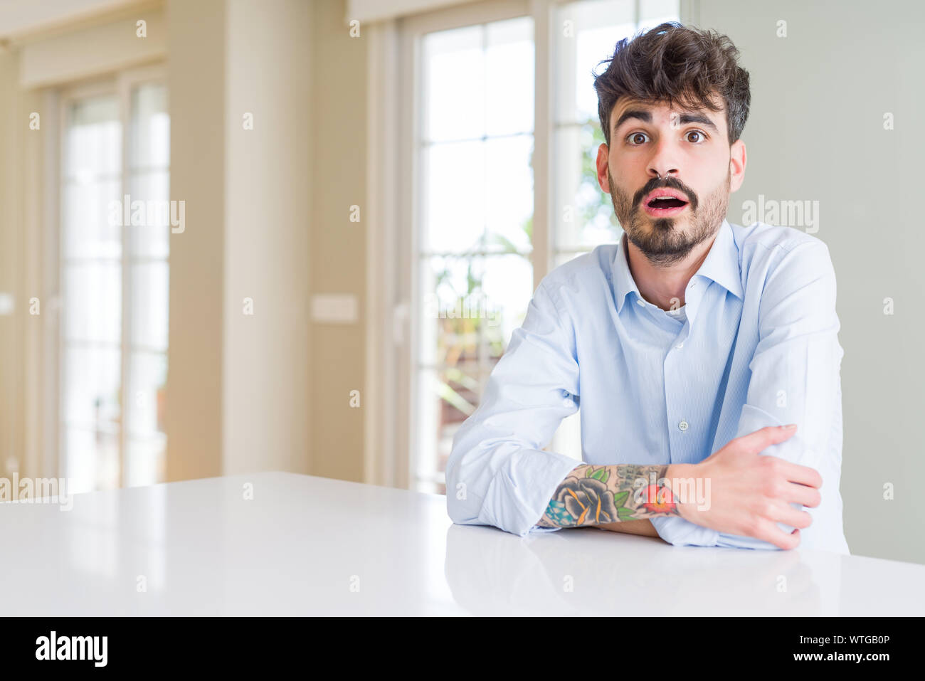 Young businesss man sitting on white table afraid and shocked with ...