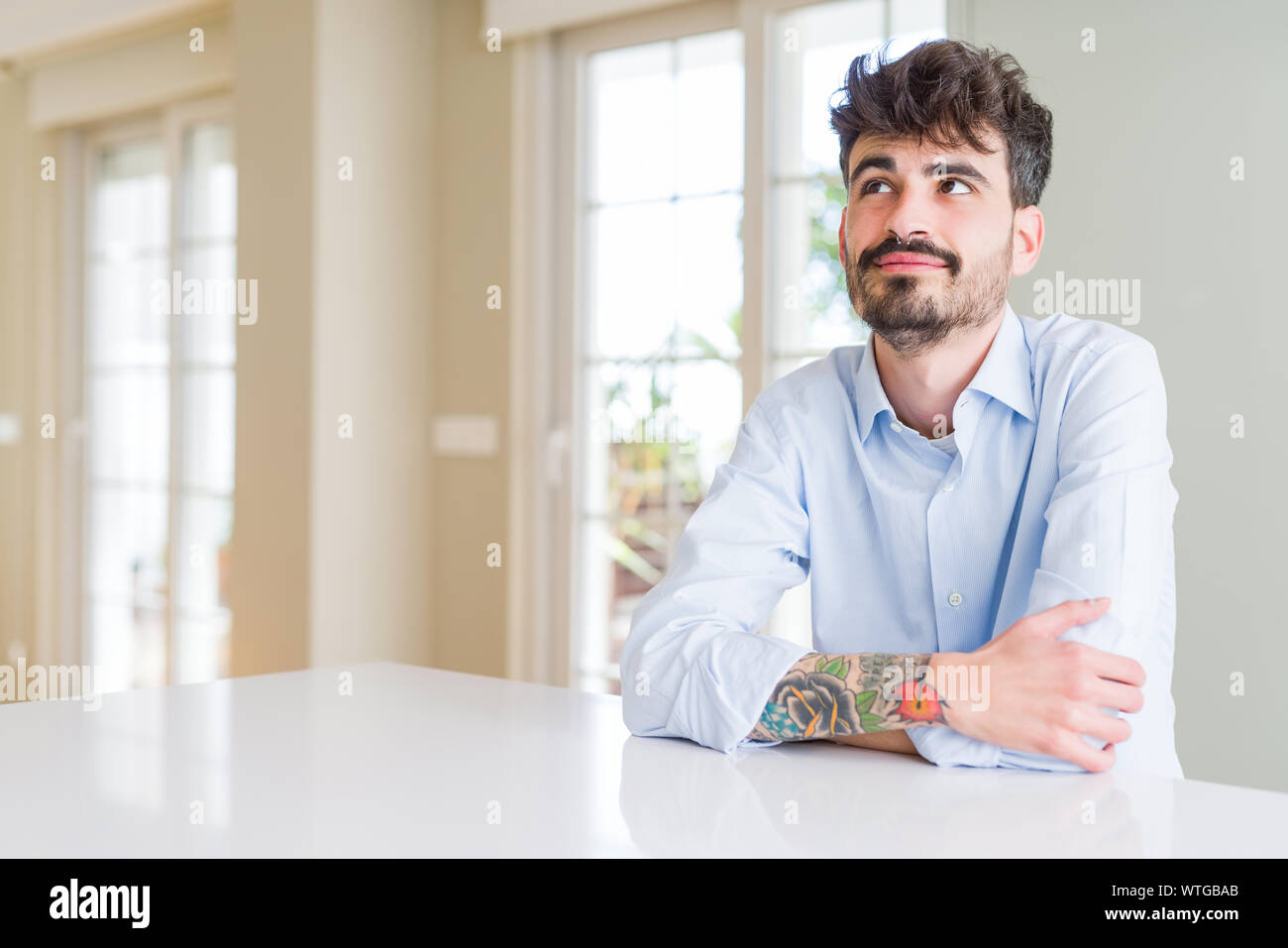 Young businesss man sitting on white table smiling looking side and ...