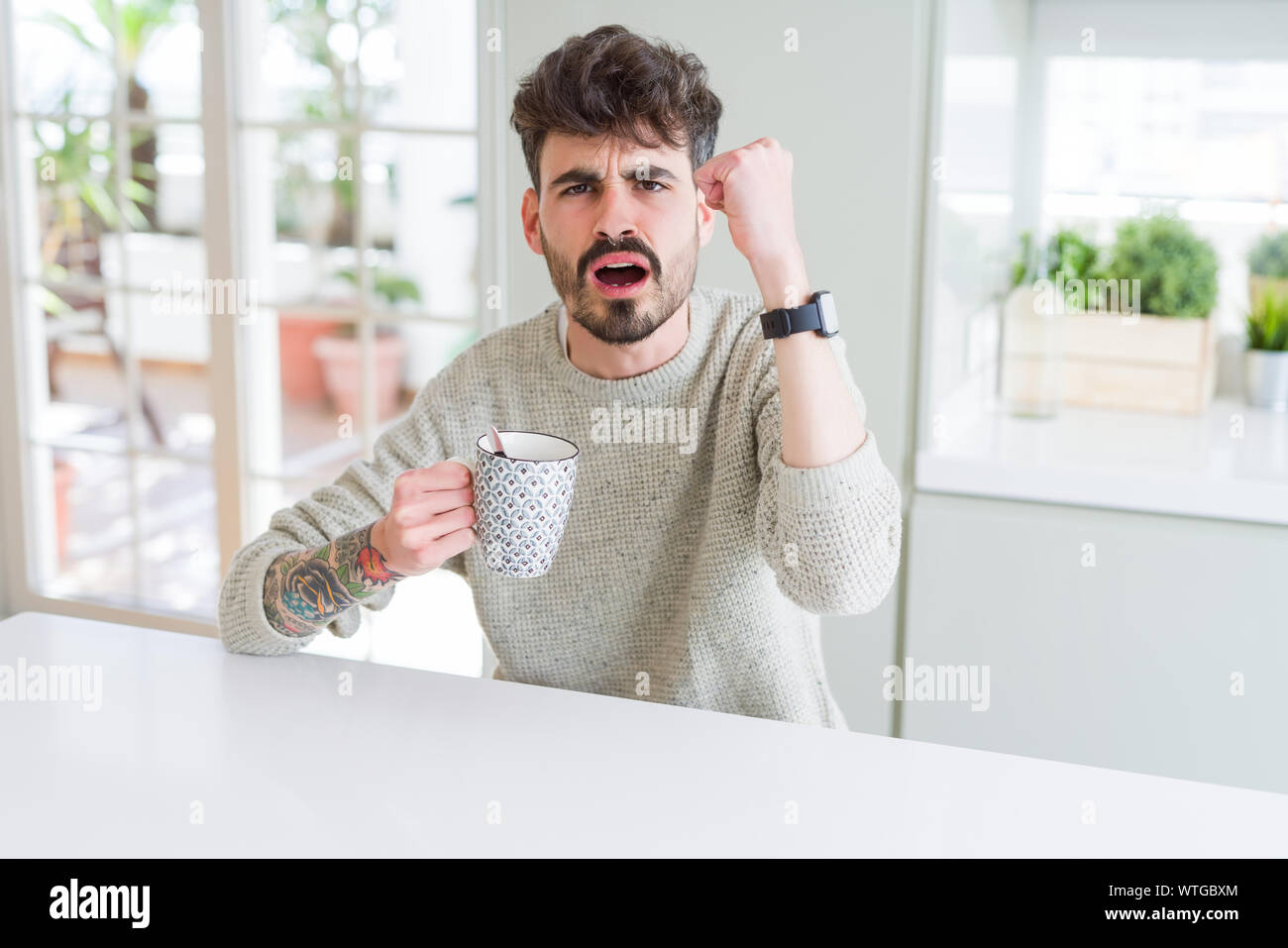 Young man drinking a cup of coffee in the morning annoyed and ...