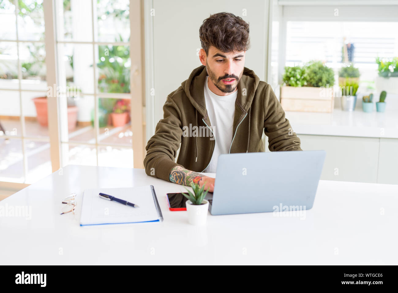 Young student man using computer laptop and notebook scared in shock ...