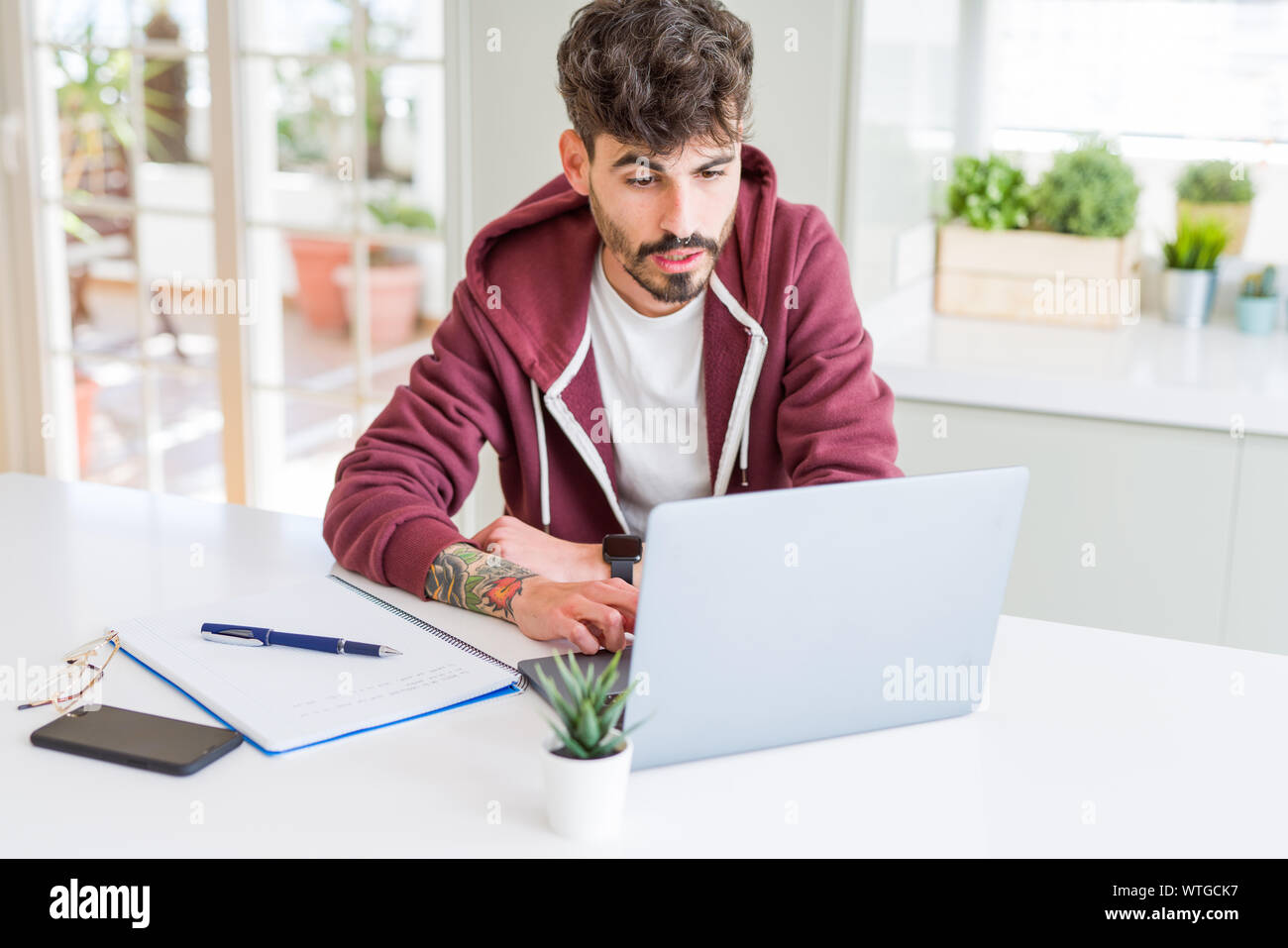 Young student man using computer laptop and notebook scared in shock ...