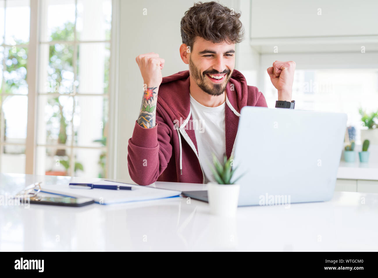 Young student man using computer laptop and notebook screaming proud ...