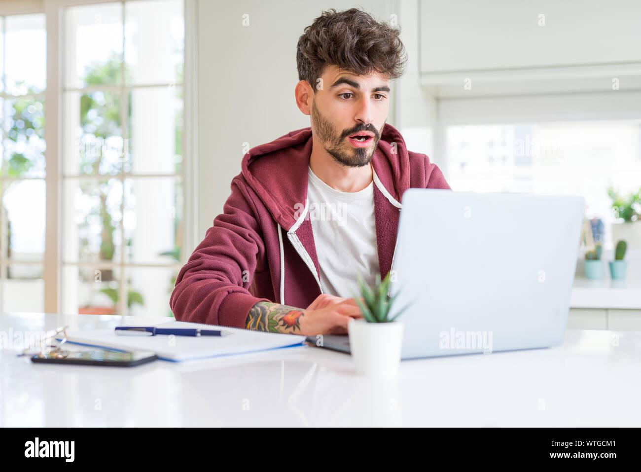 Young student man using computer laptop and notebook scared in shock ...