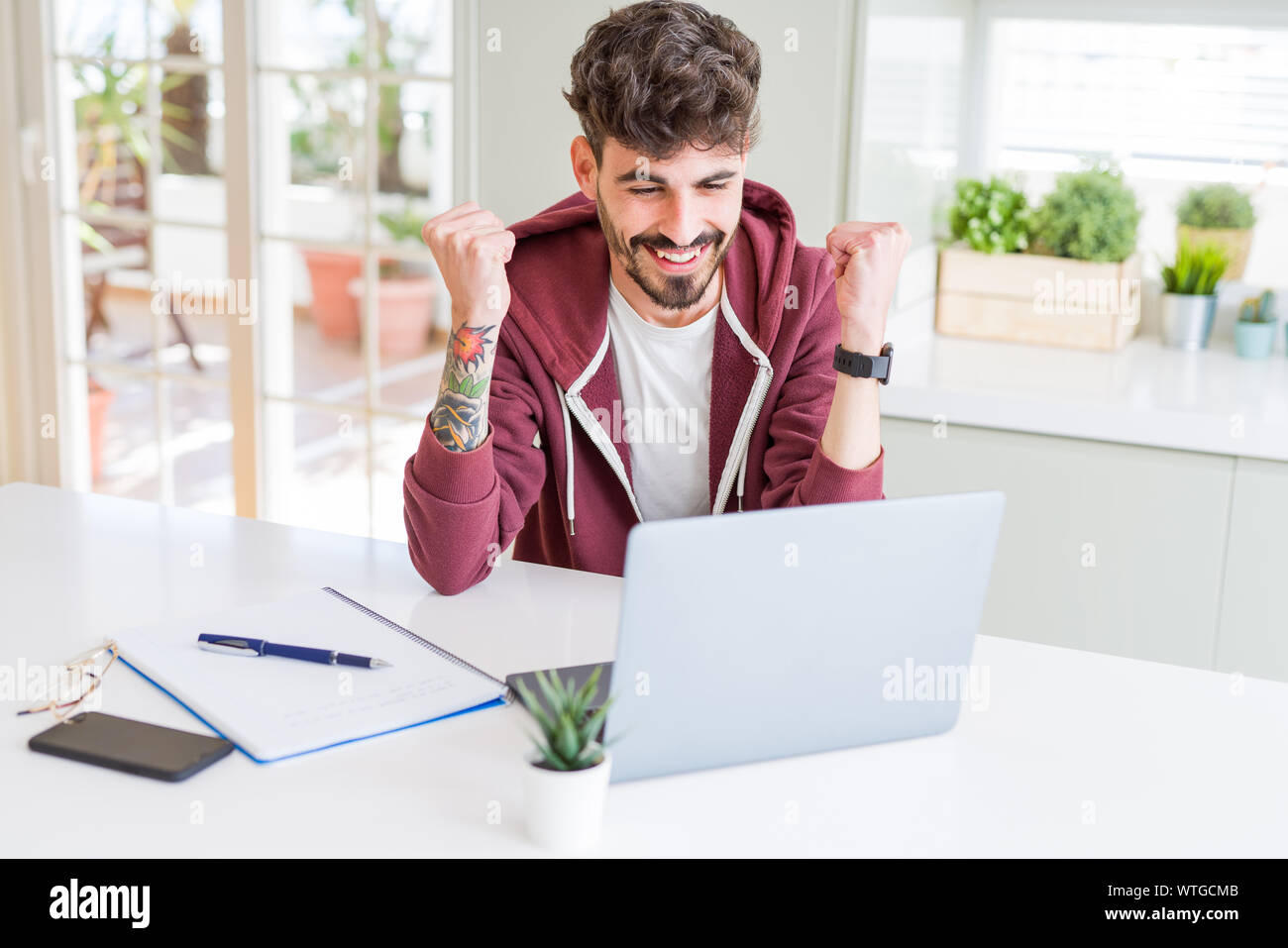 Young student man using computer laptop and notebook screaming proud ...