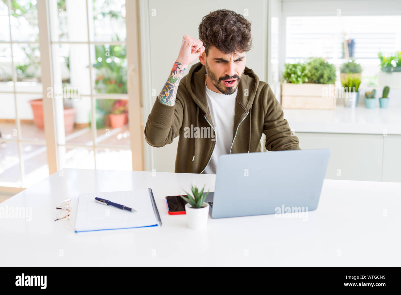 Young student man using computer laptop and notebook annoyed and ...