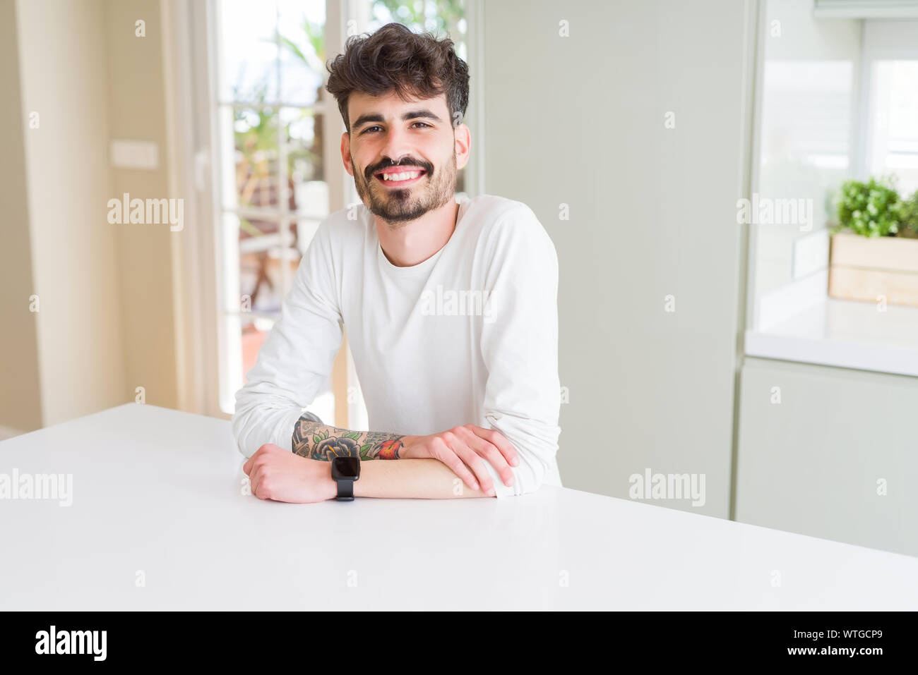 Handsome young man smiling cheerful at the camera with crossed arms and ...